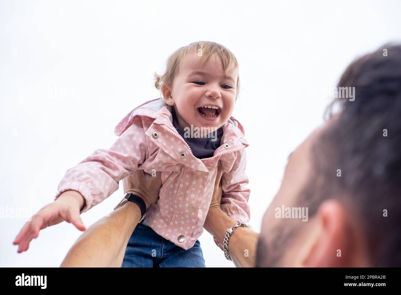Low angle view of a happy little girl lifting in arms of her dad ...