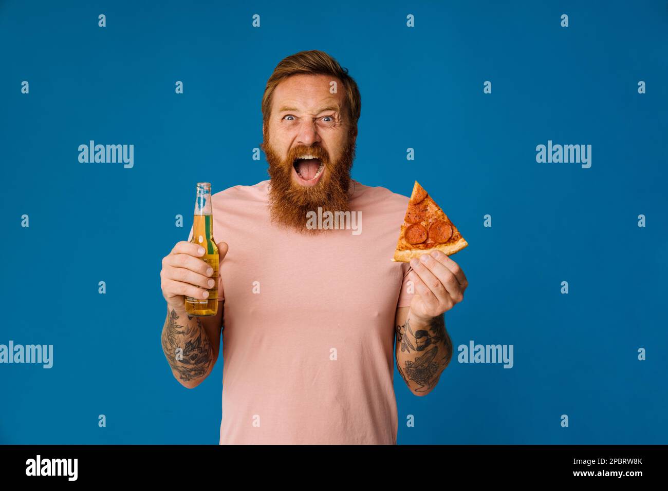 Angry screaming ginger man holding pizza and beer isolated over blue ...