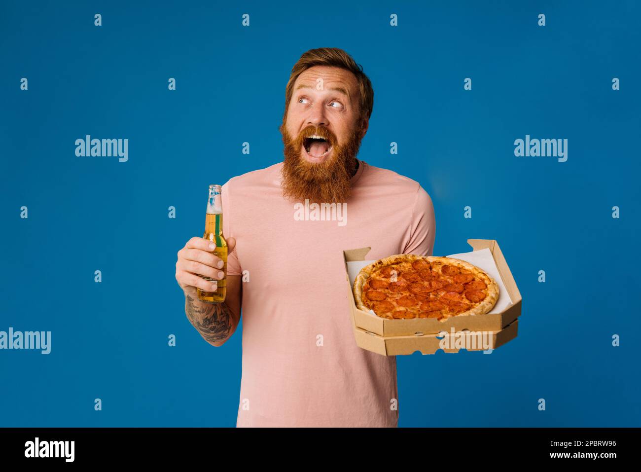 Happy screaming ginger man holding pizza and beer isolated over blue ...
