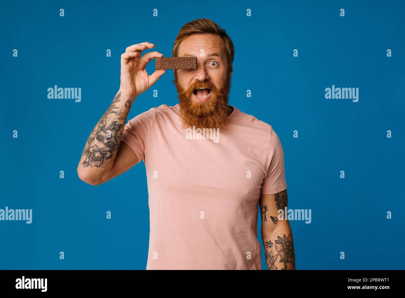 Excited white bearded man covering his eye with candy bar isolated over ...