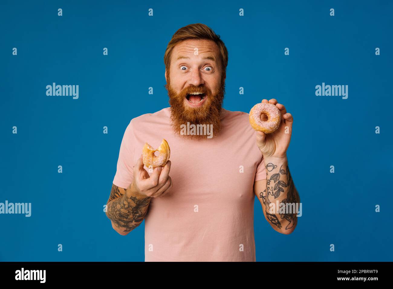 Excited screaming bearded man in casual wear holding donuts isolated ...