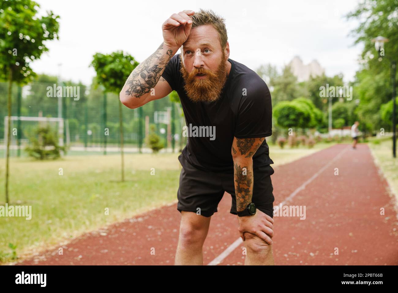 Portrait of adult bearded redhead man leaning on his knee, wiping sweat ...
