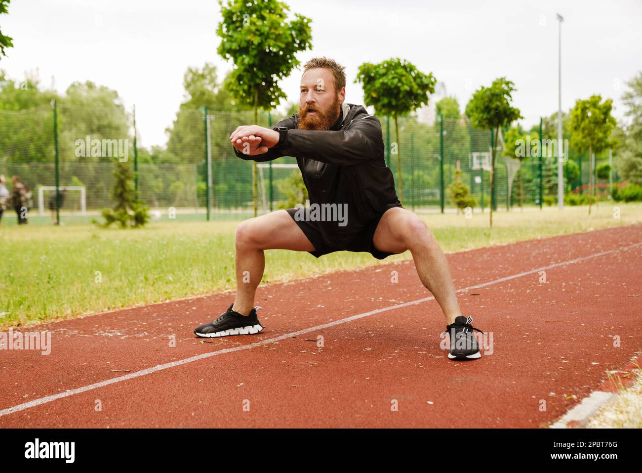 Adult handsome bearded redhead man doing deep squats looking aside ...