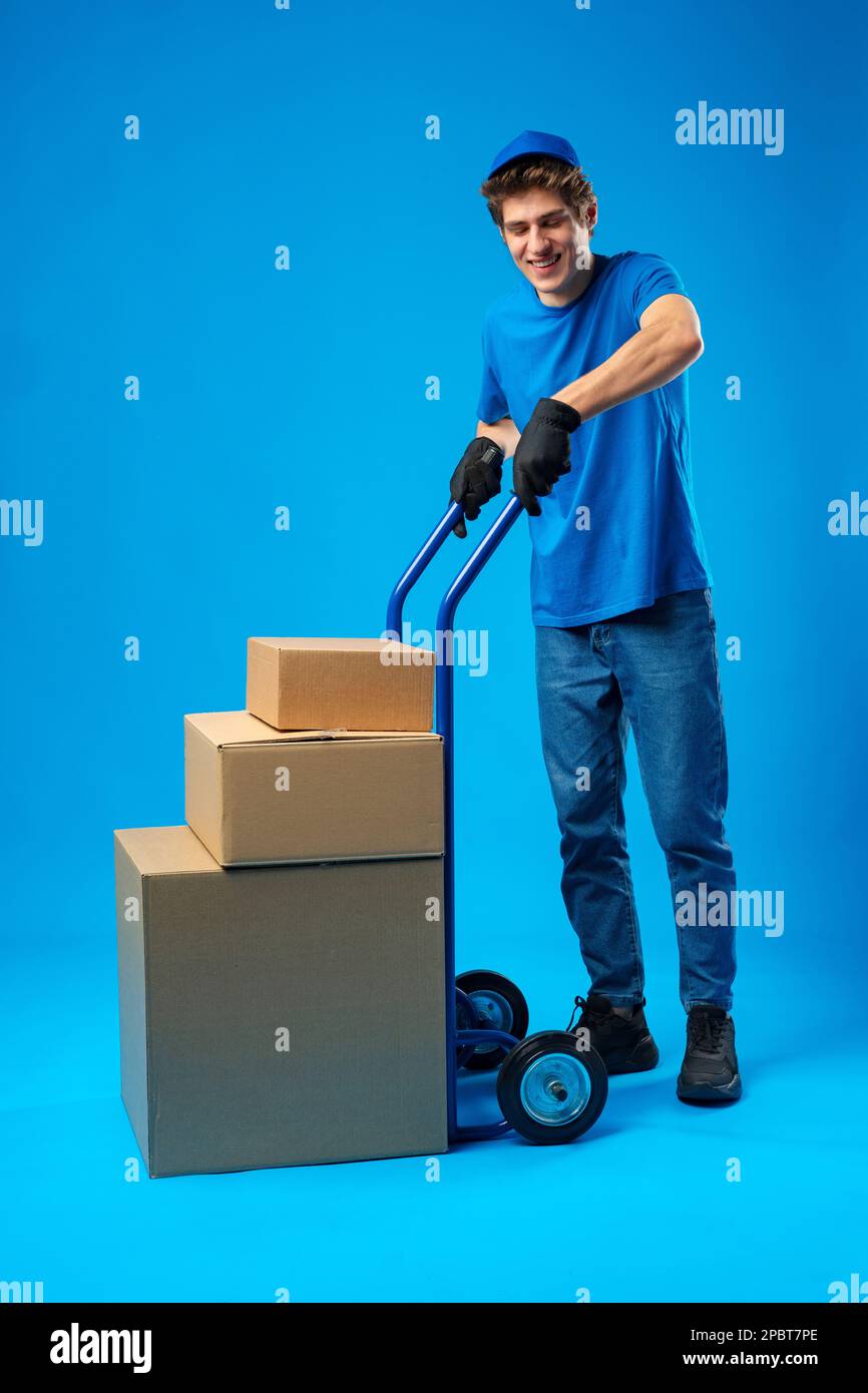 Young happy delivery man carrying boxes on truck against blue ...