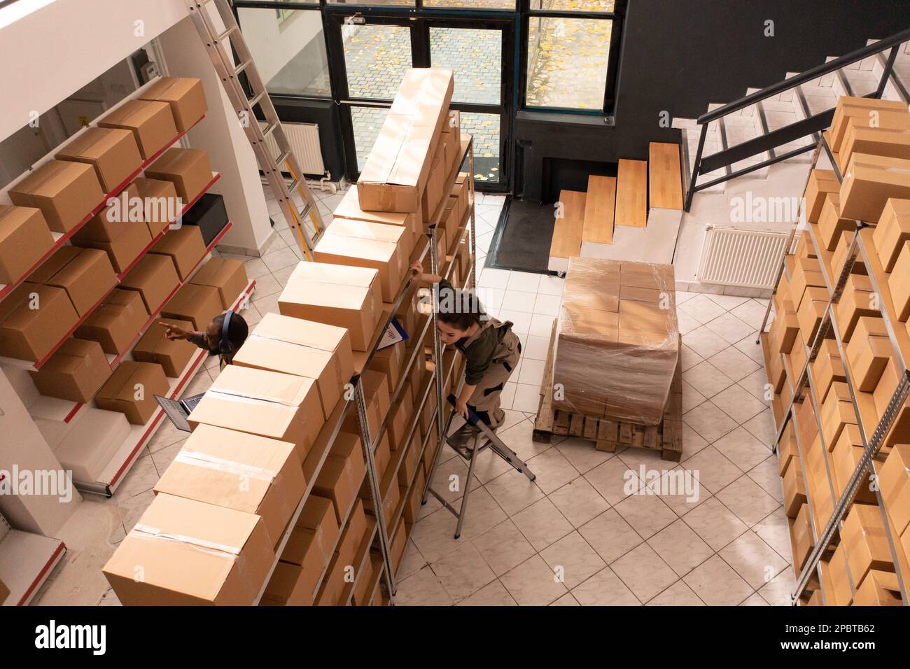 Stockroom worker standing on ladder checking carton boxes, preparing ...