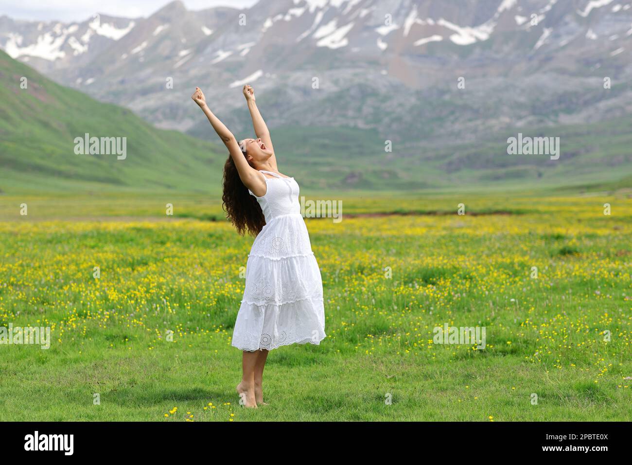 Excited woman in white dress raising arms in nature Stock Photo - Alamy