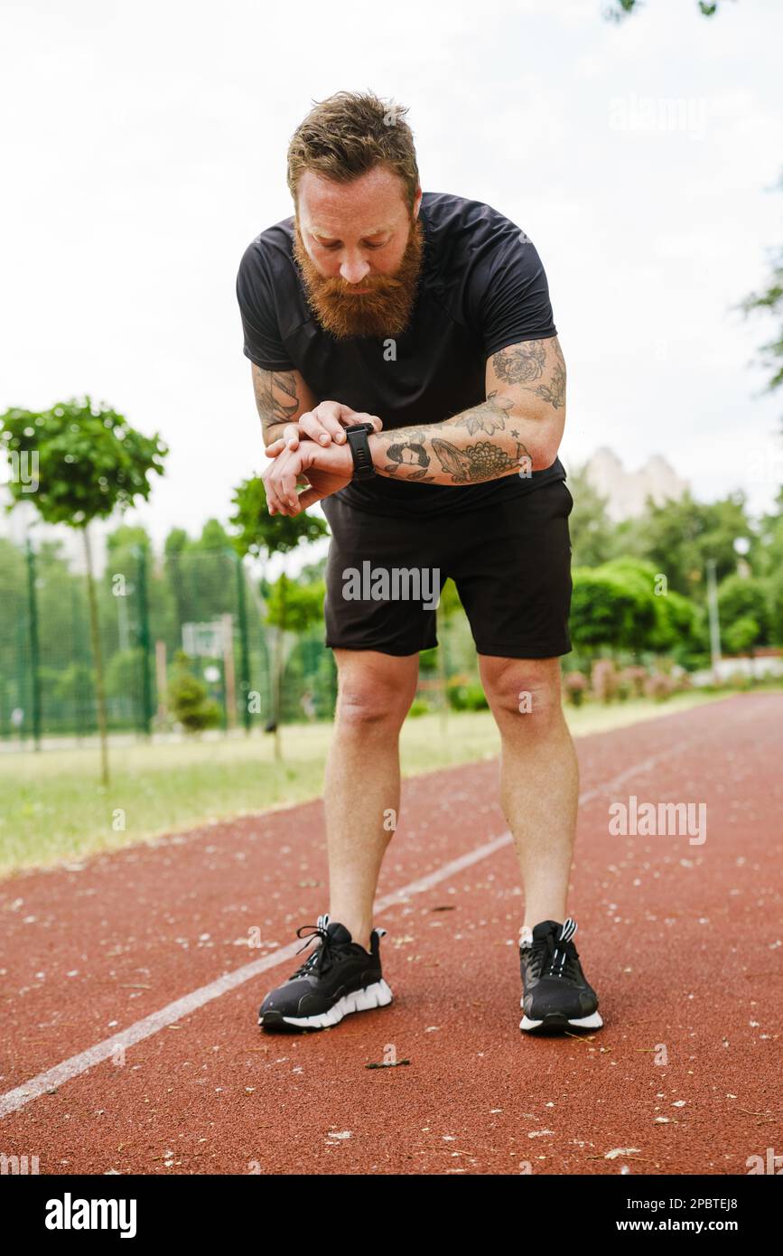 Ginger bearded sportsman using smartwatch while working out in park ...