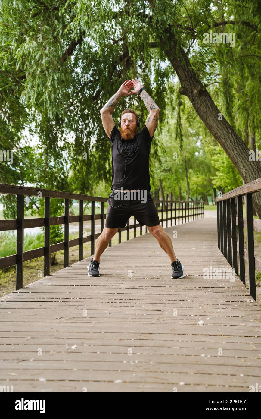 Ginger bearded sportsman doing exercise while working out in park ...