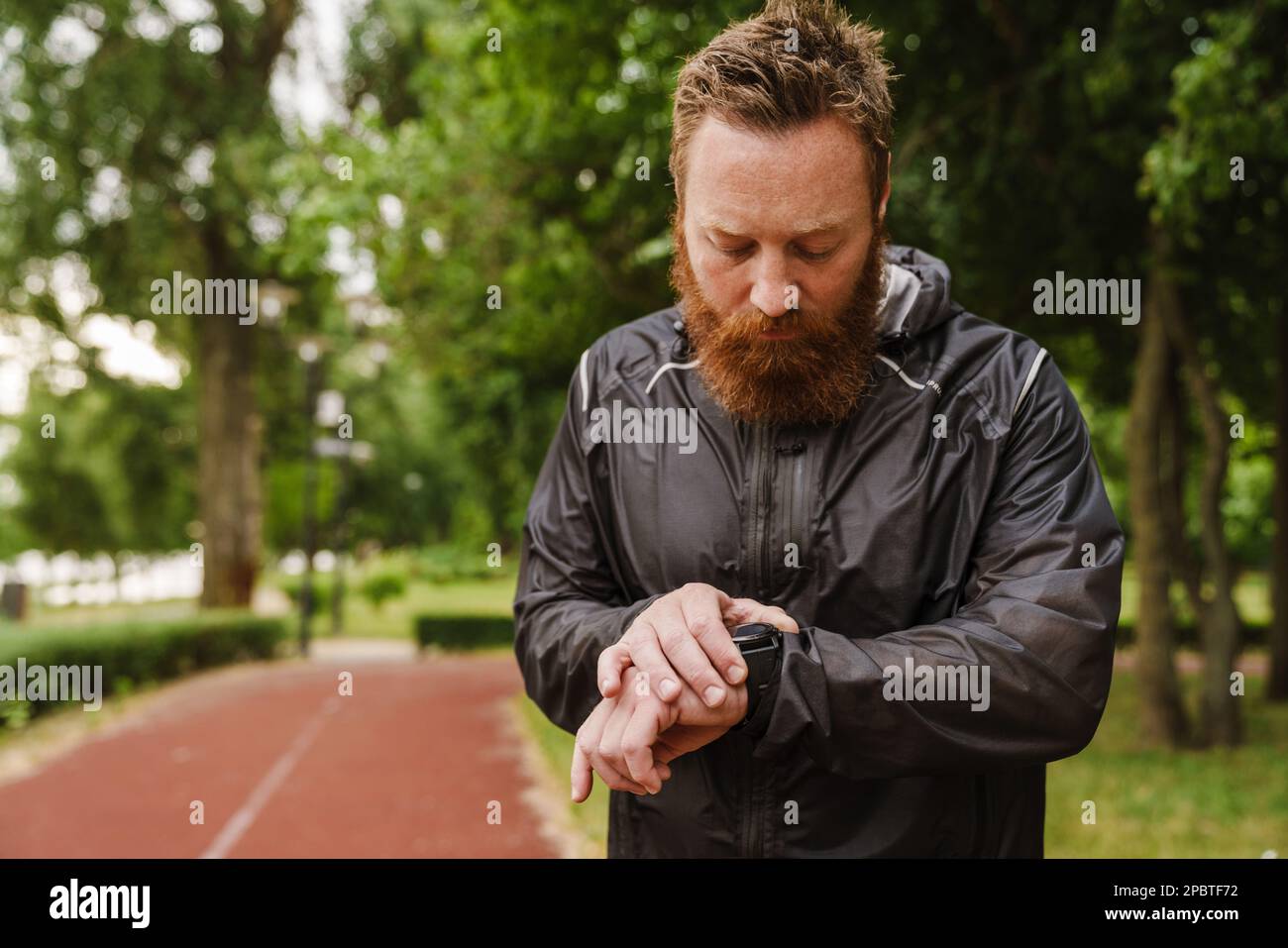Ginger bearded sportsman using smartwatch while working out in park ...