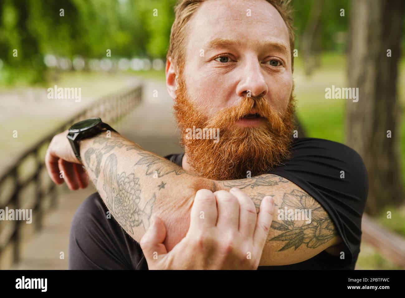 Ginger bearded sportsman doing exercise while working out in park ...