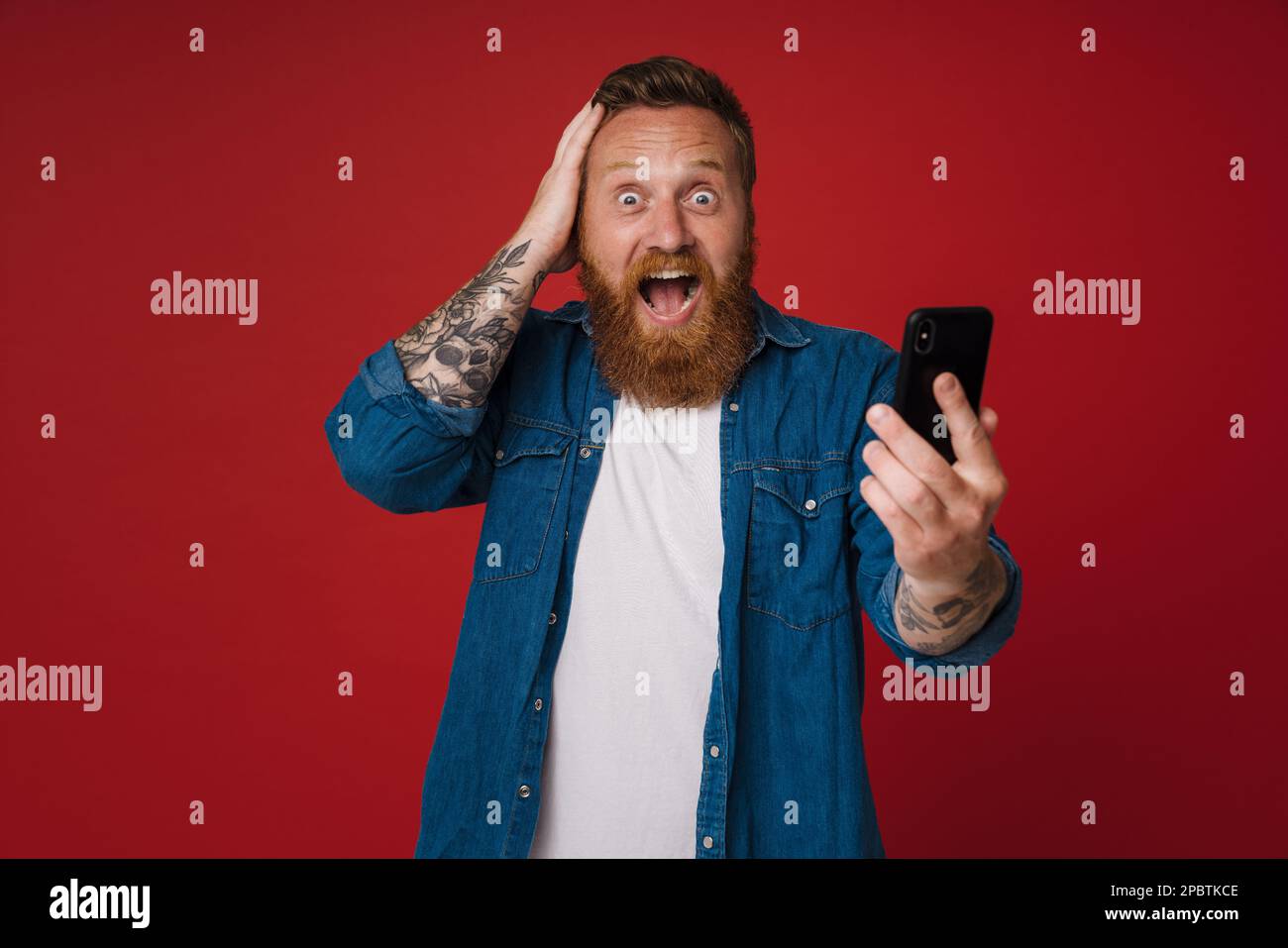 Ginger excited man wearing denim shirt using cellphone and gesturing ...
