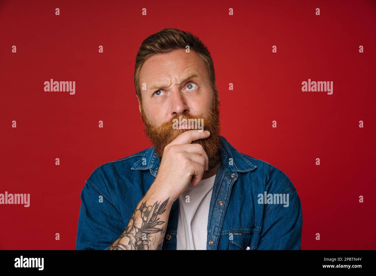 Ginger puzzled man with tattoo frowning and looking upward isolated ...