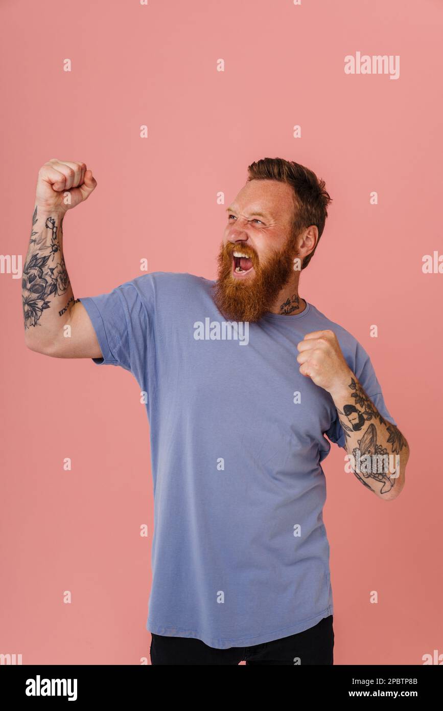 Ginger white man screaming and making winner gesture isolated over pink ...