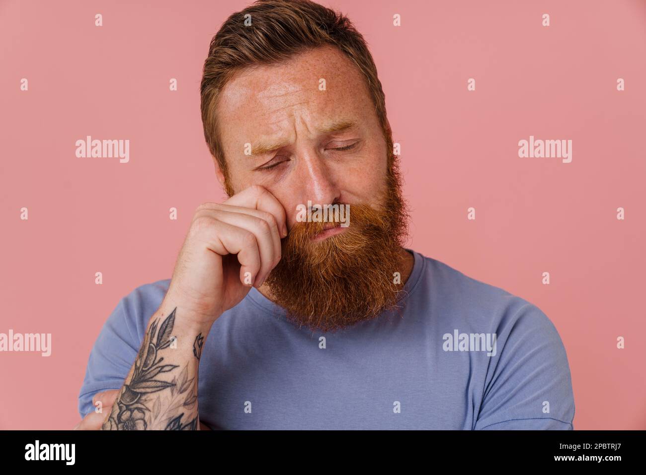 Ginger sad man with beard crying while wiping his tears isolated over ...