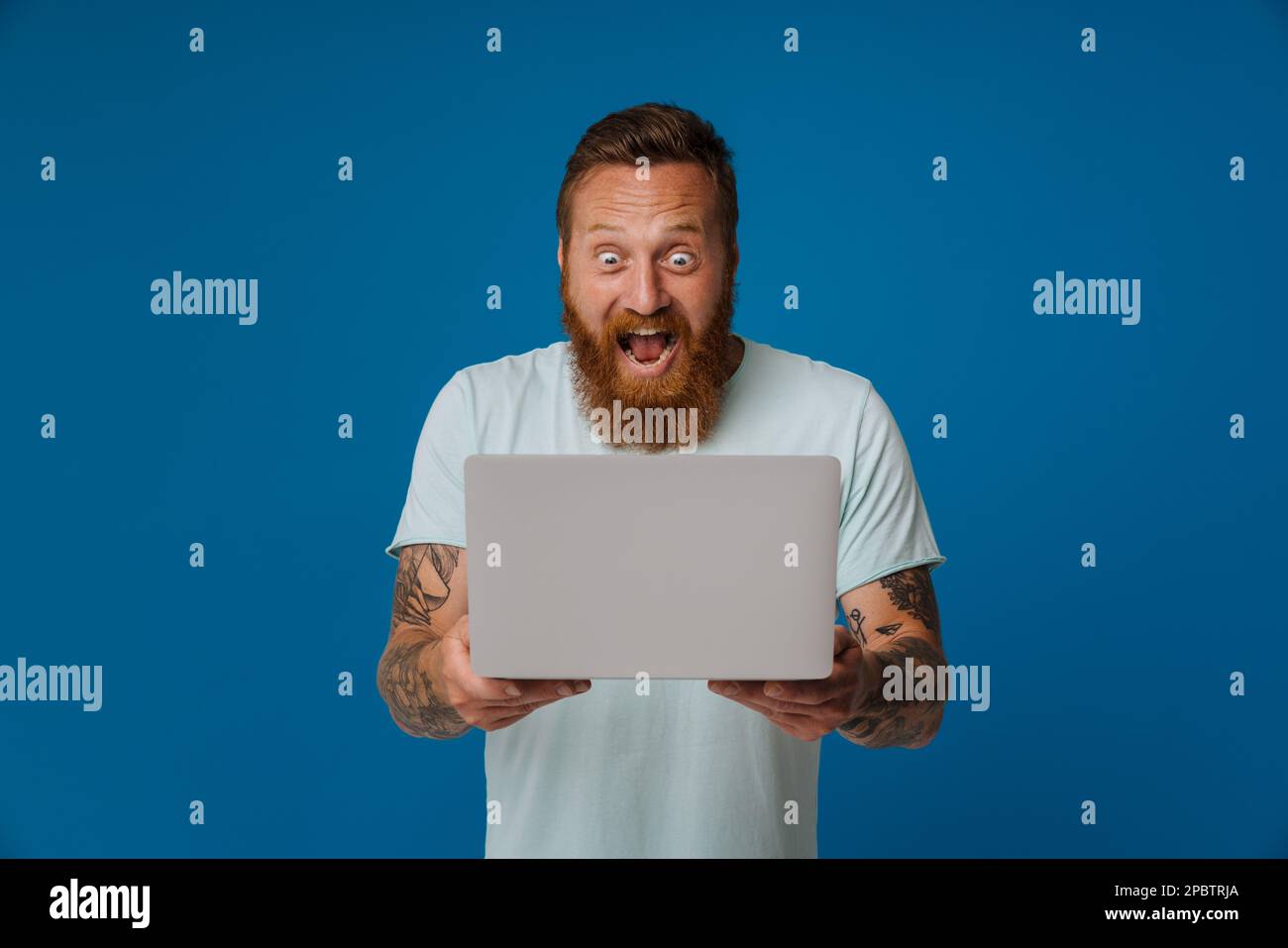 Ginger excited man with tattoo screaming and working with laptop ...