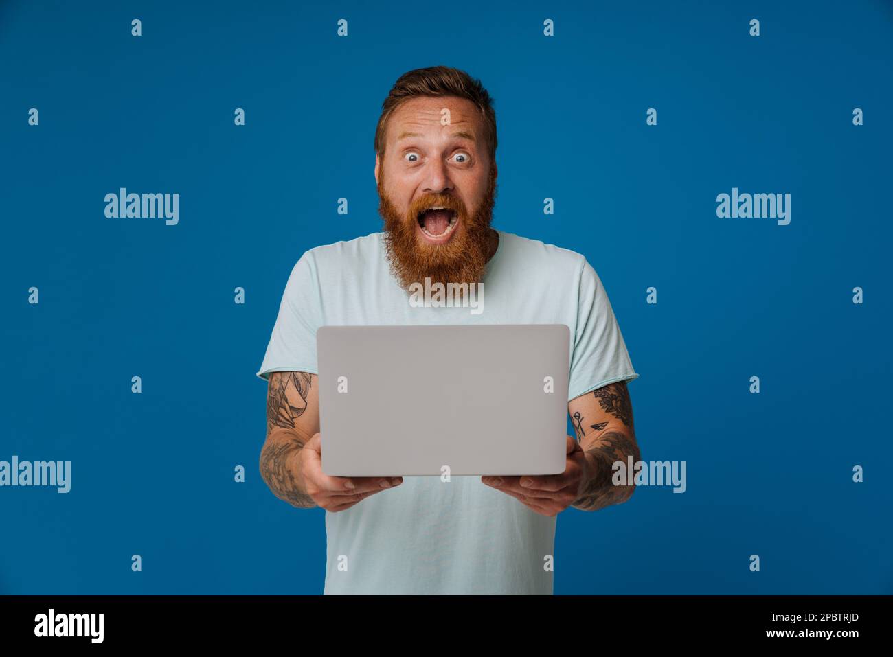 Ginger excited man with tattoo screaming and working with laptop ...