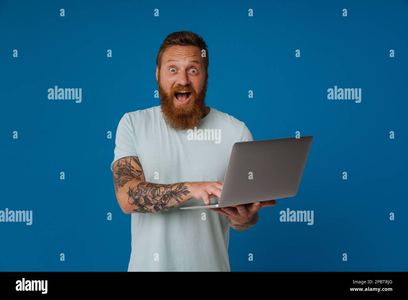 Ginger excited man with tattoo screaming and working with laptop ...