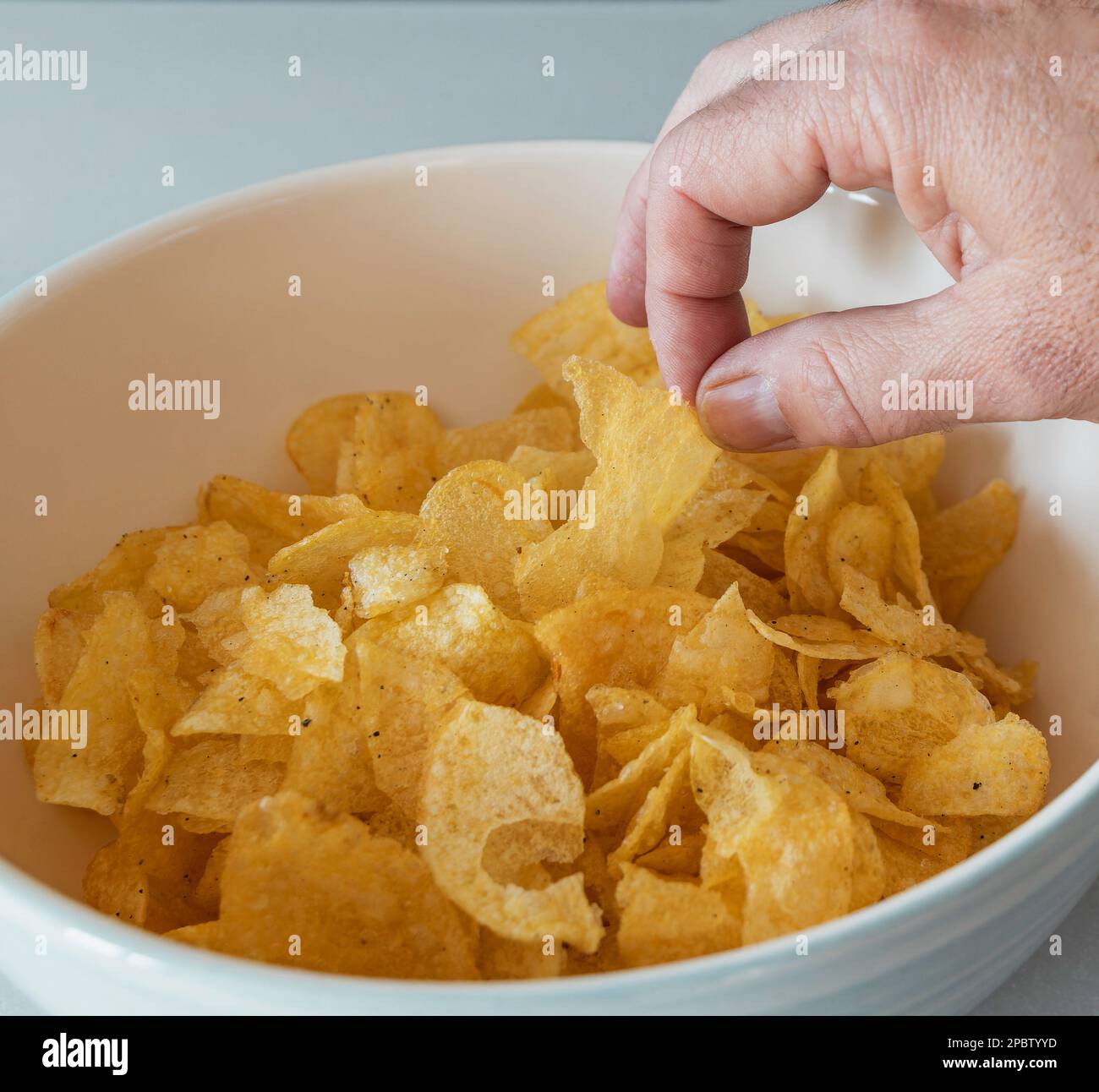 a man's hand reaching potato chips in white ceramic bowl Stock Photo ...
