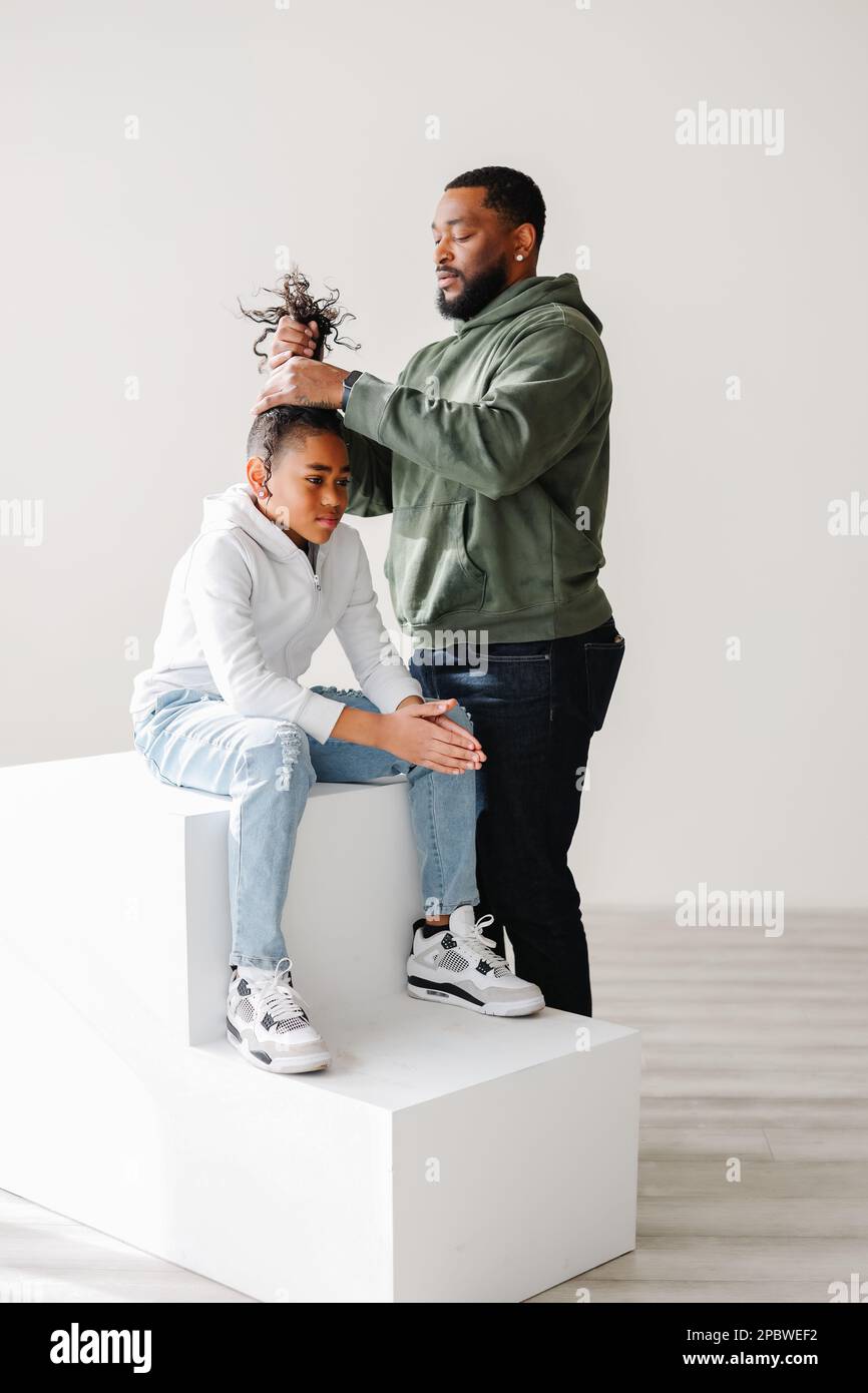 Stylish Black dad doing mixed race son's hair inside Stock Photo - Alamy