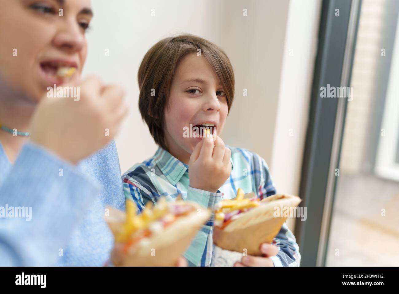 Cute little boy eating gyros together with his mother. Portrait of ...