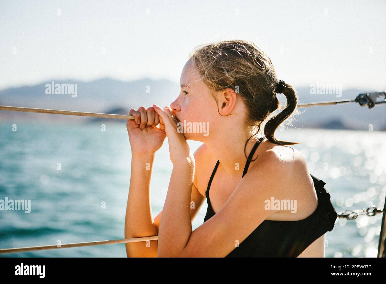 Tween girl in swimsuit on edge of boat overlooking water in sunshine ...
