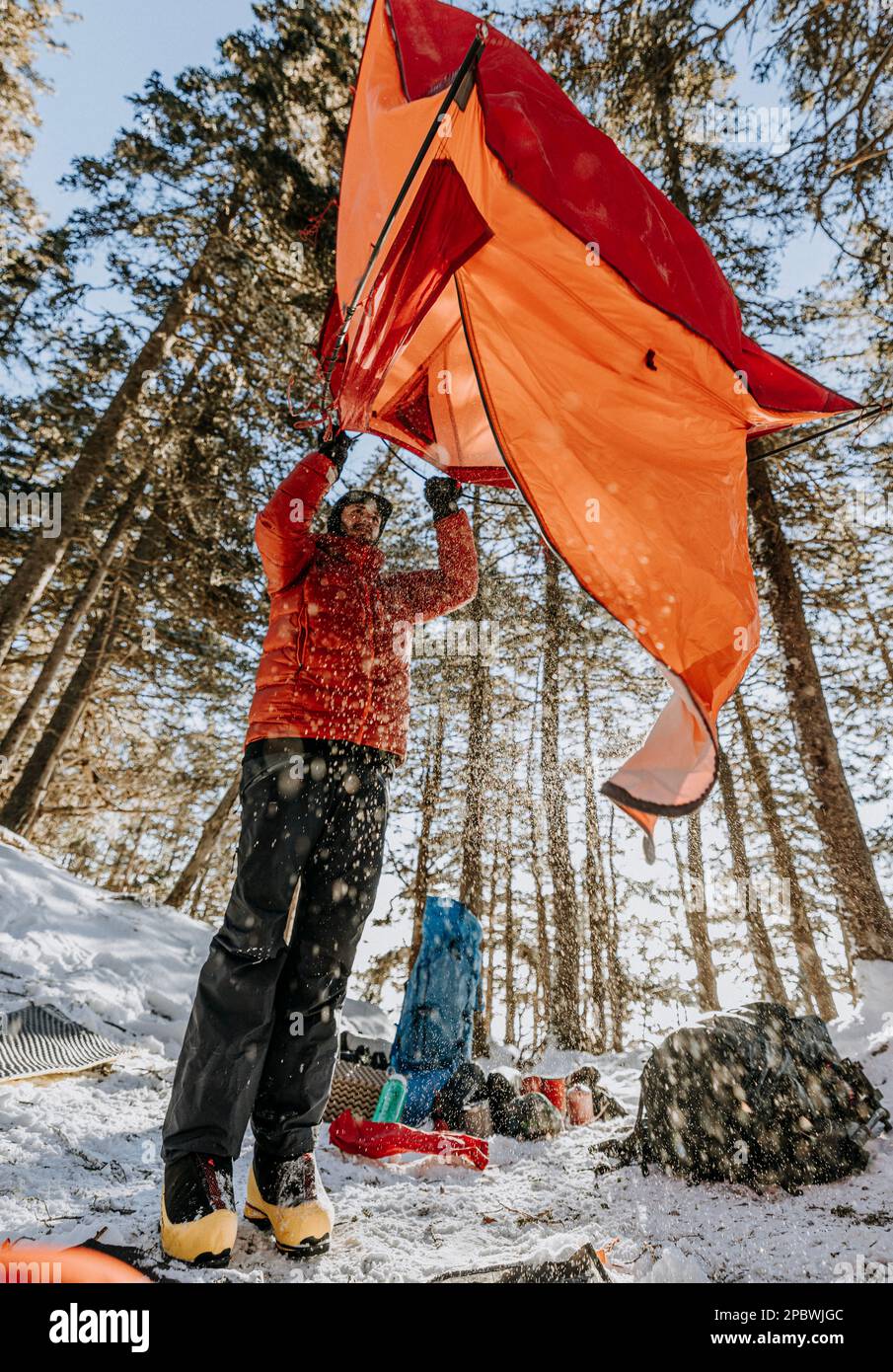 Man shakes frost and snow off tent while winter camping in Maine Stock ...
