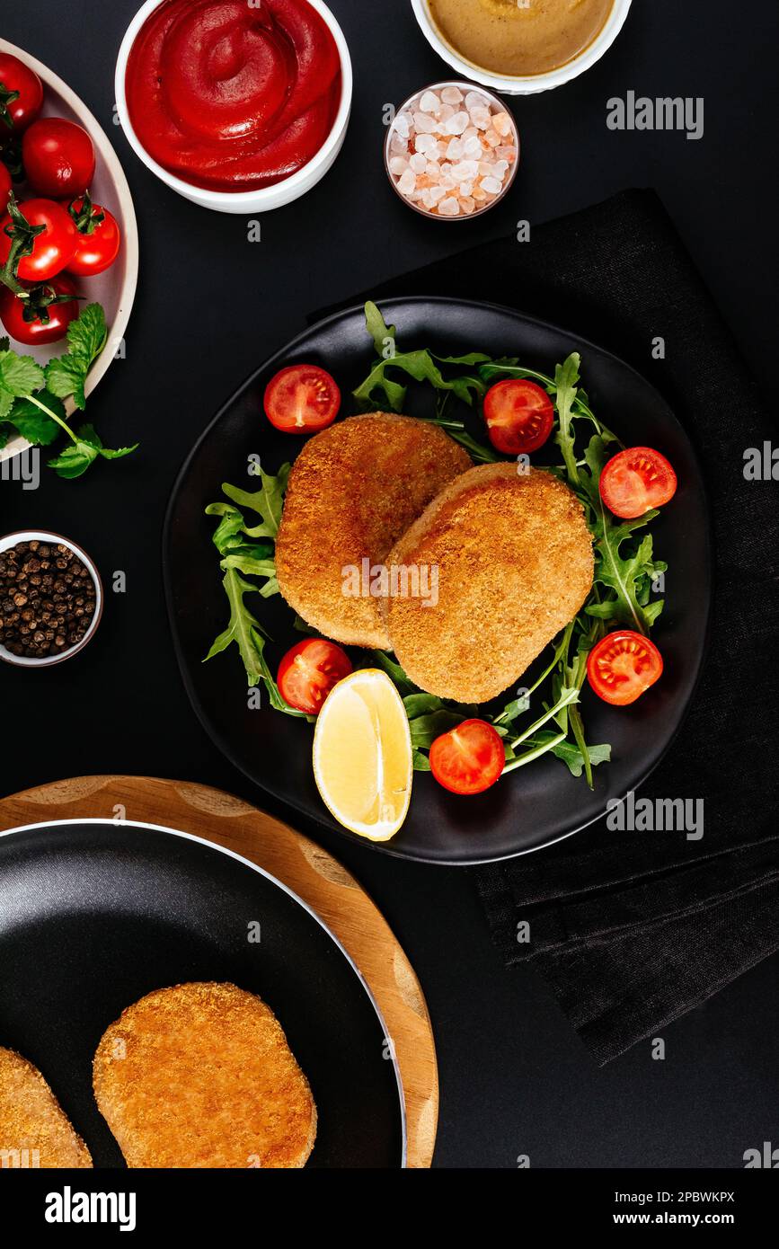 chicken cutlet on a black plate. vegetables and herbs. black bac Stock ...