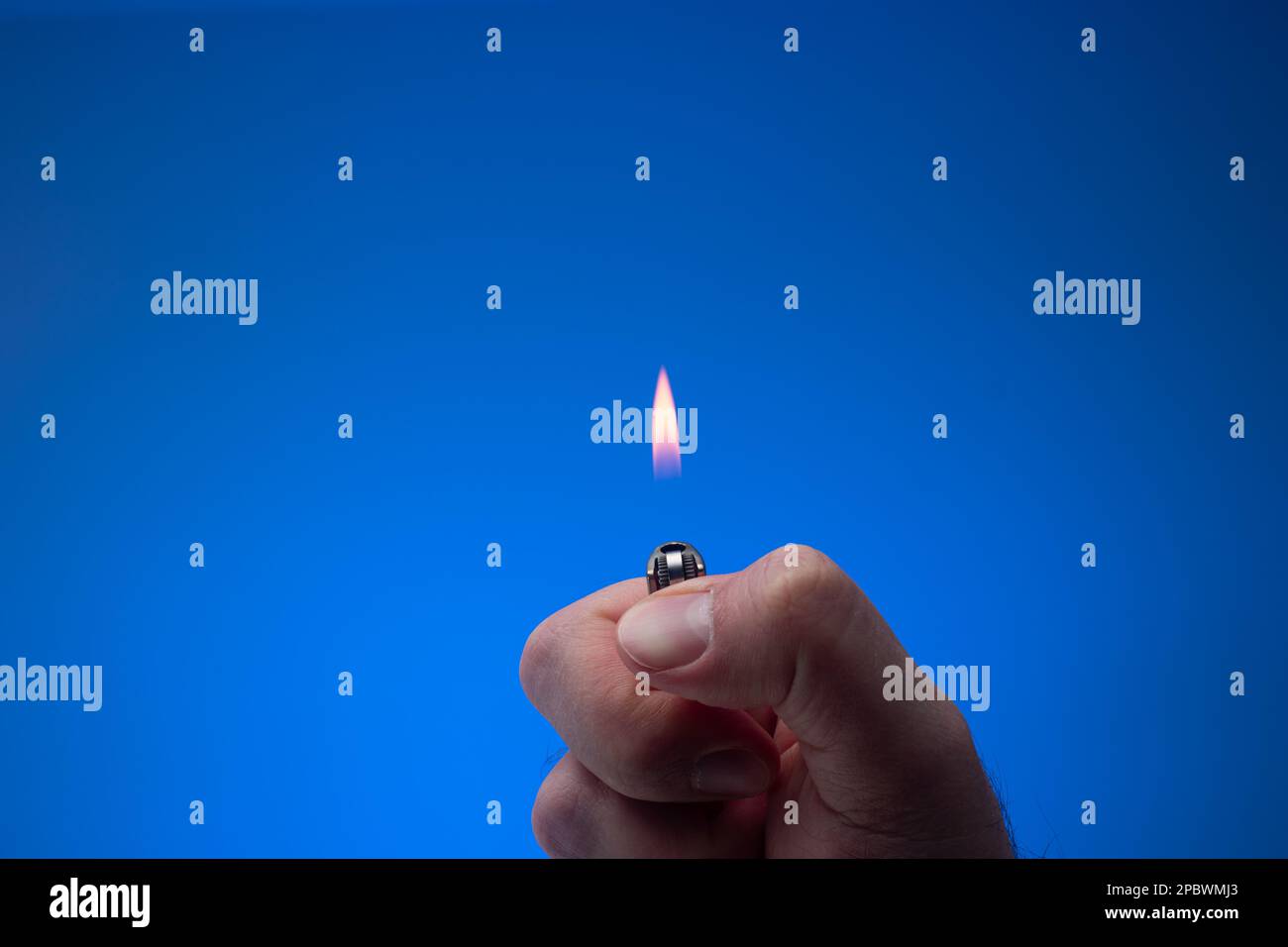 Lit small lighter with flame held between fingers by man. Close up ...