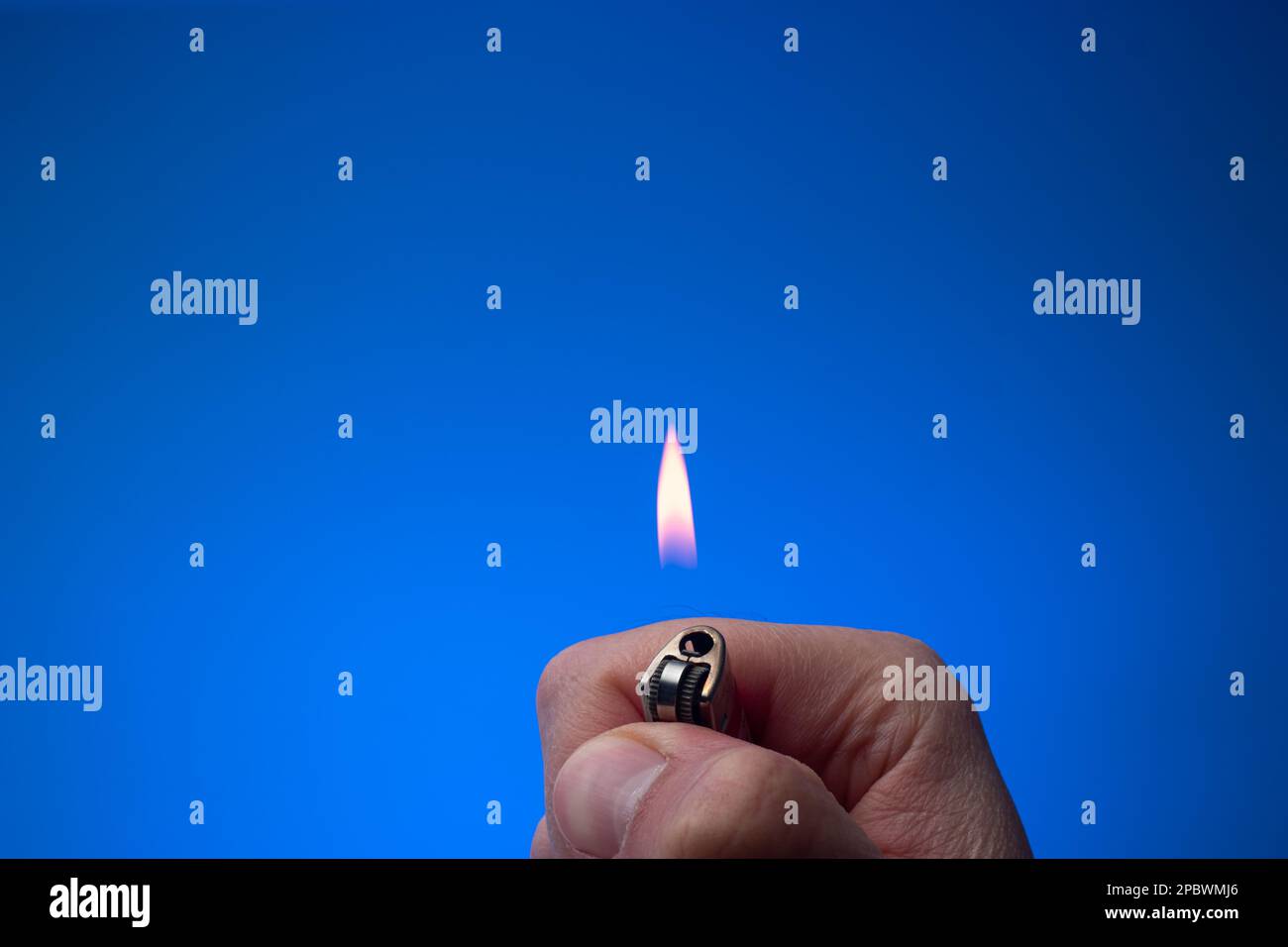 Lit small lighter with flame held between fingers by man. Close up ...