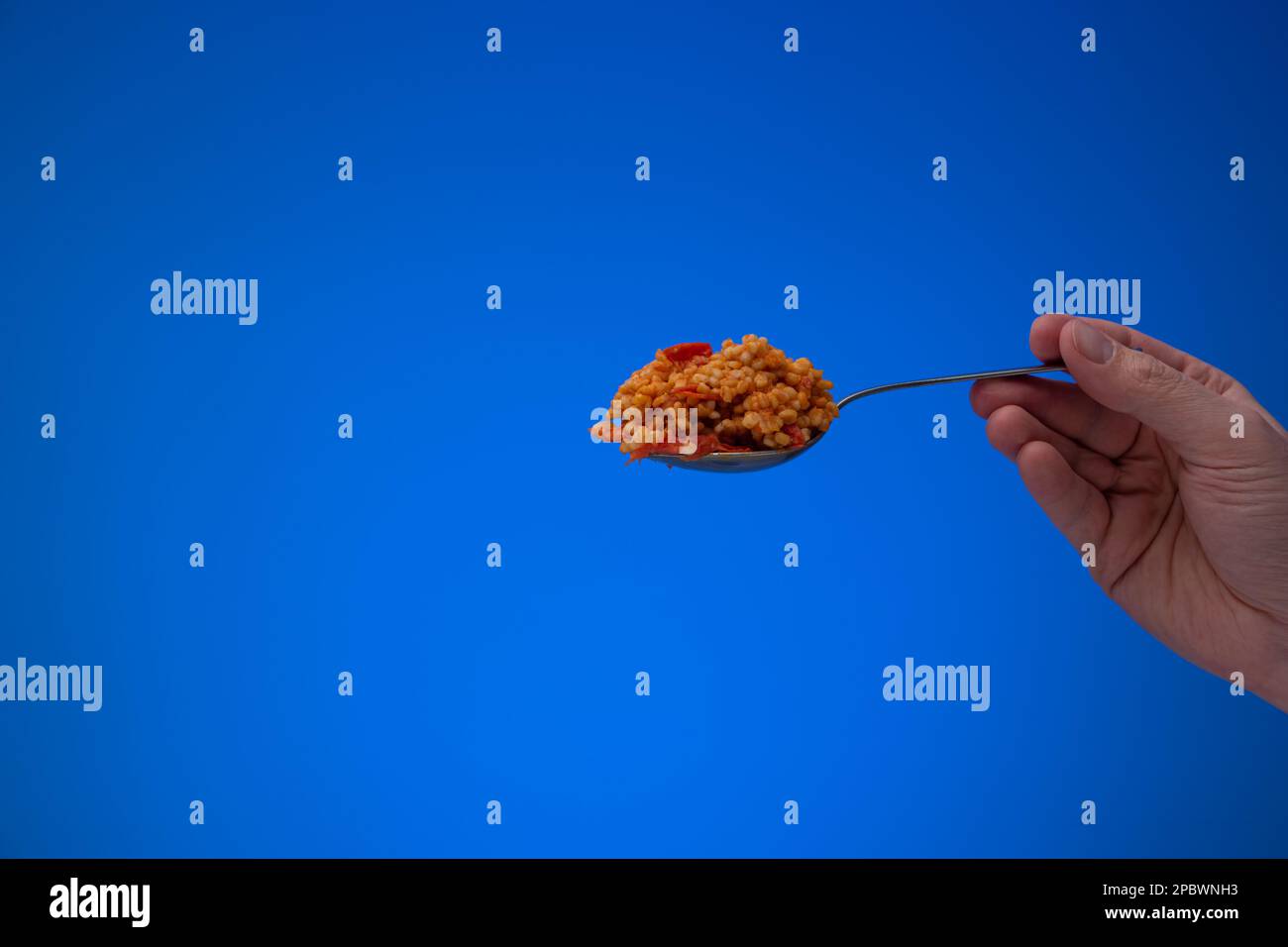 Cooked bulgur with diced tomatoes on a silver spoon held by Caucasian ...