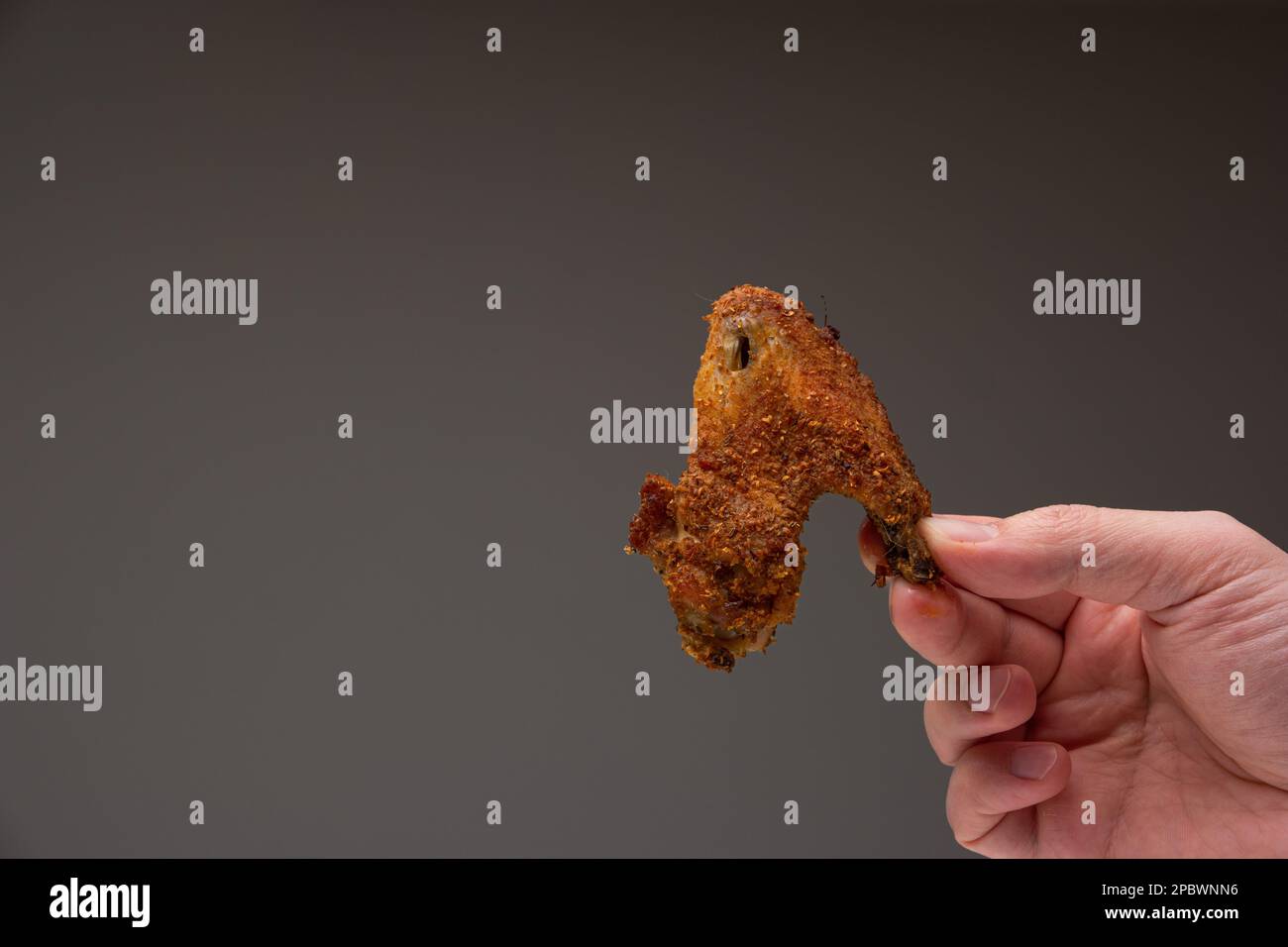 Grilled and seasoned chicken wing held between fingers by Caucasian ...