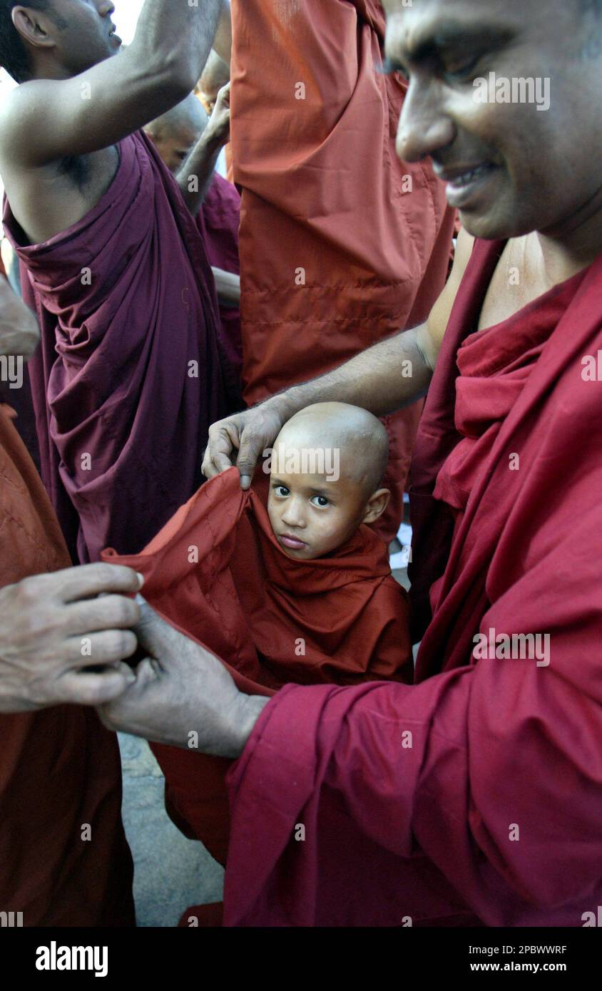 Buddhist monks help a young novice monk with tying his robe during a ...