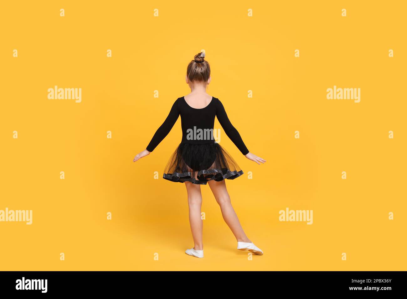 Cute little girl in black dress dancing on yellow background, back view ...