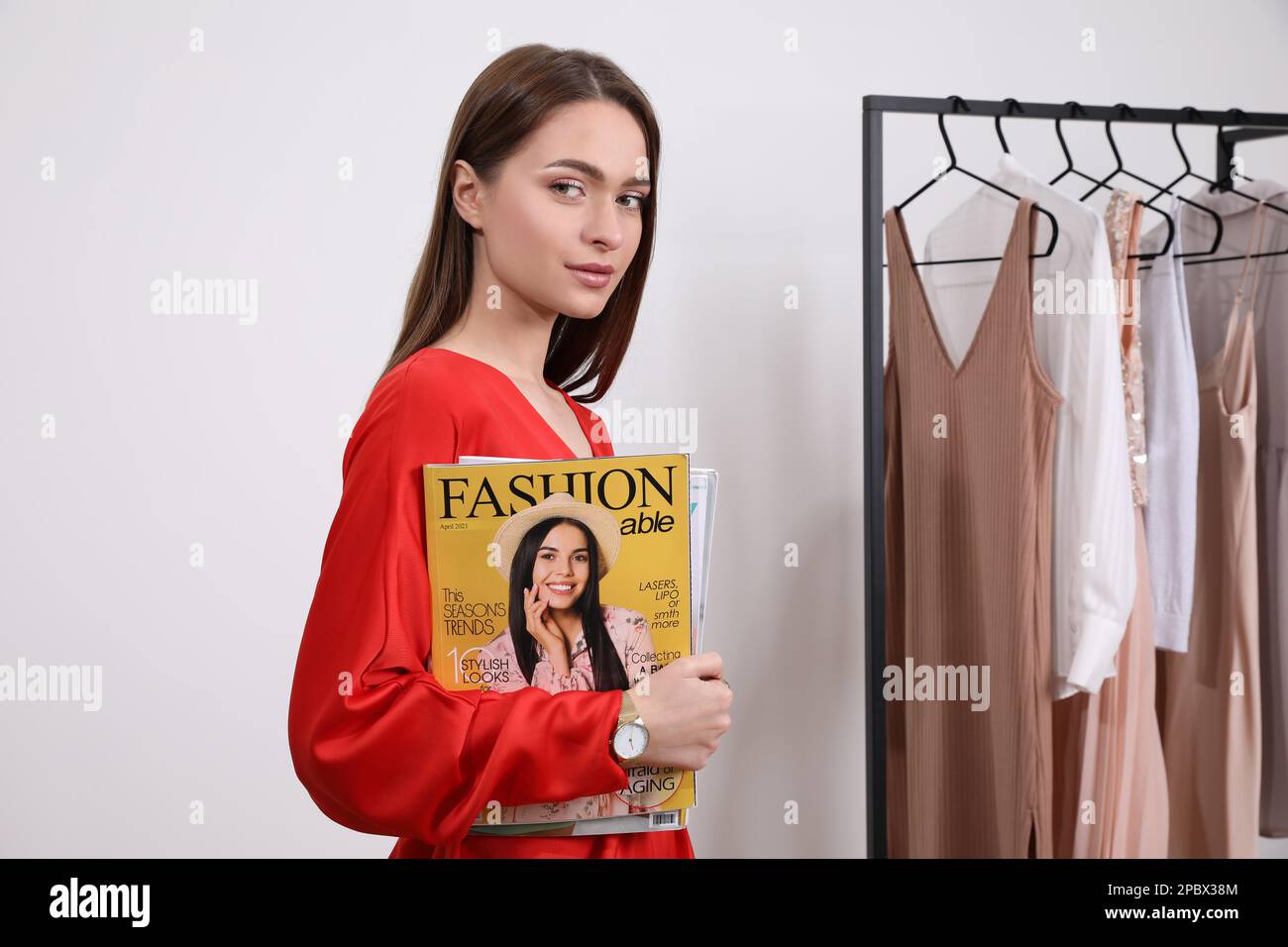 Young woman with fashion magazine near clothes rack indoors Stock Photo ...