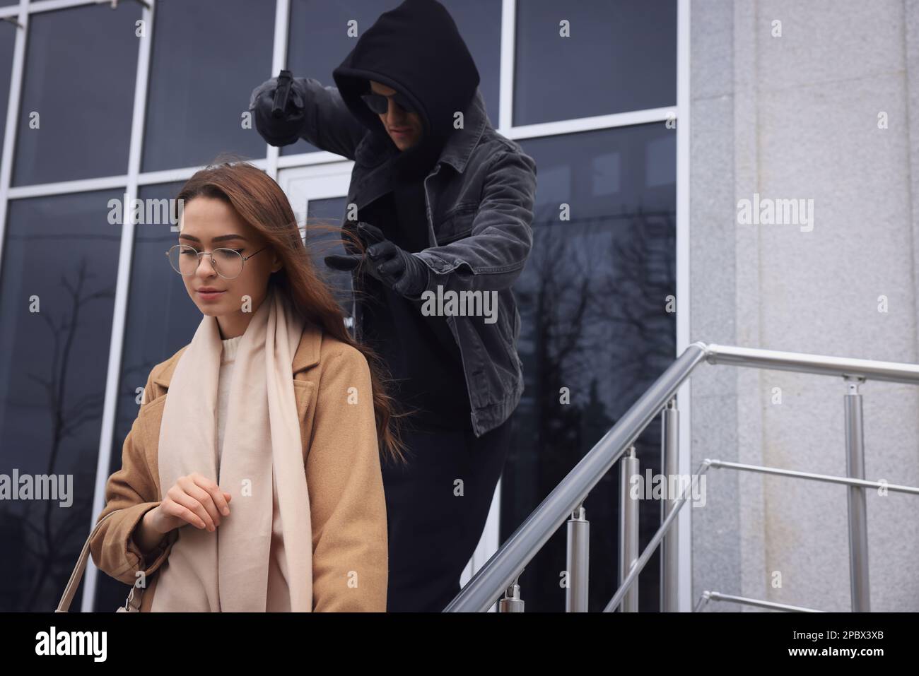 Criminal with gun attacking young woman near building Stock Photo - Alamy