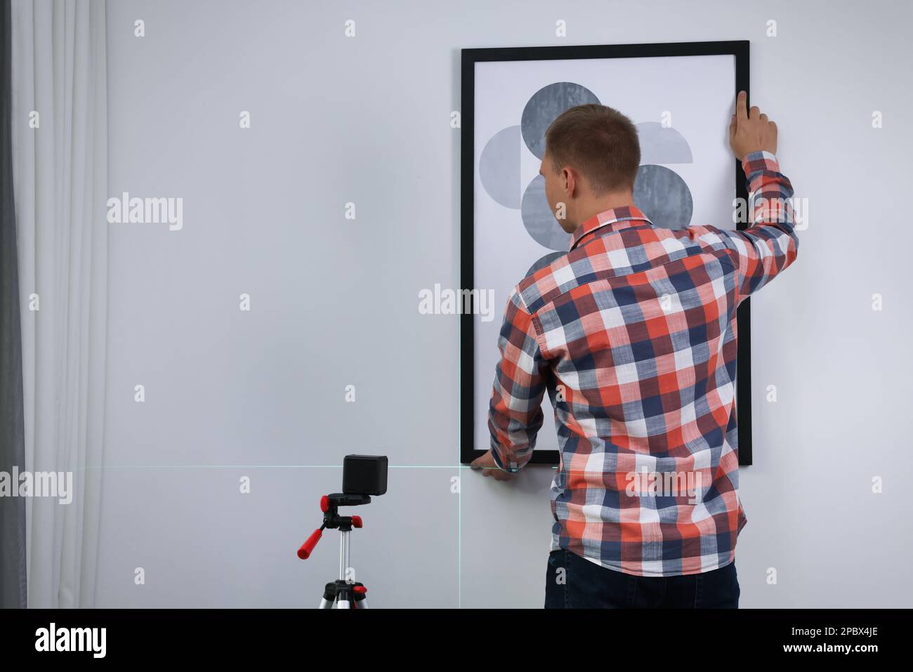 Man using cross line laser level for hanging painting on light wall ...