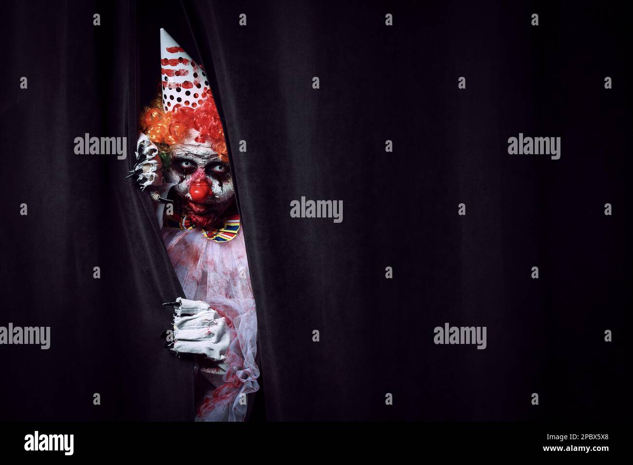Terrifying clown hiding behind black curtains, space for text ...