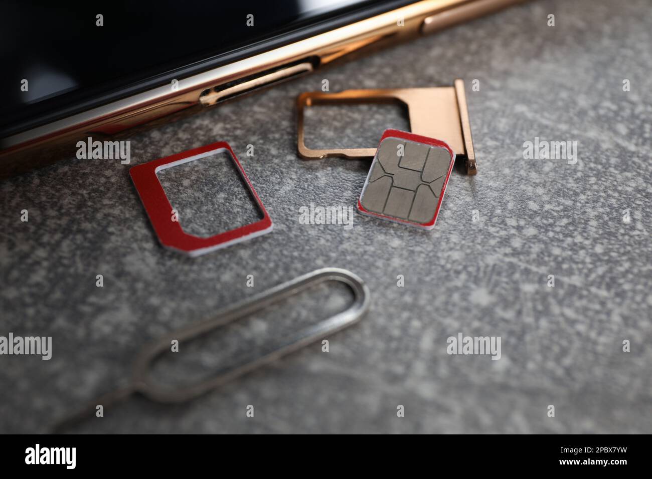 SIM card, mobile phone, tray and ejector tool on grey table, closeup ...