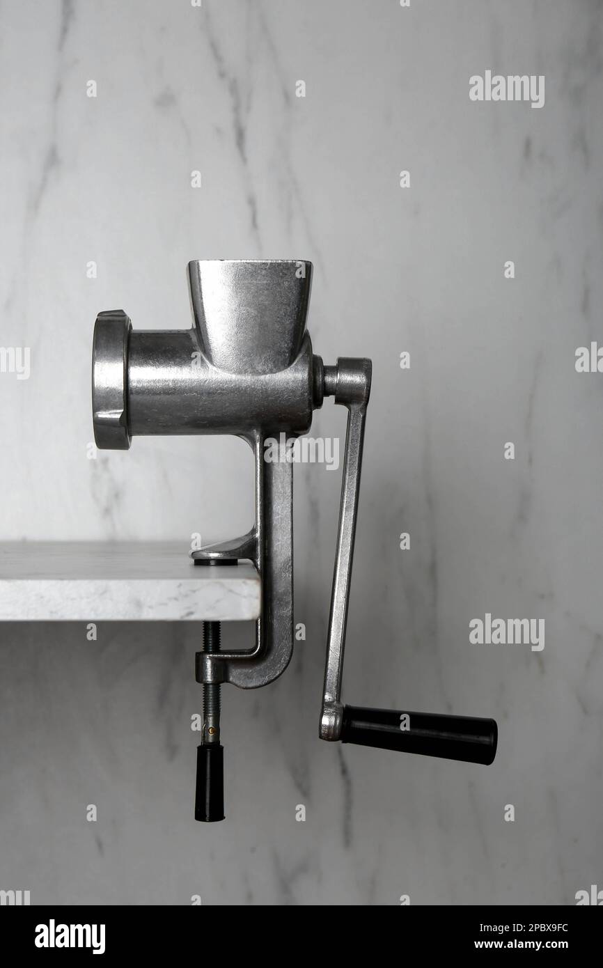 Metal manual meat grinder on table against white marble background ...