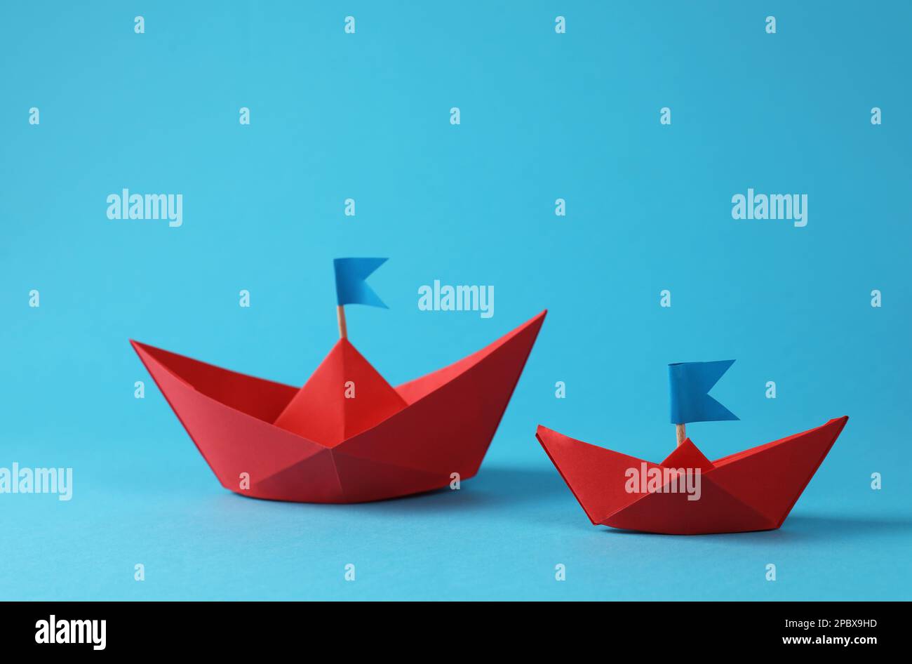 Two handmade red paper boats with flags on light blue background ...