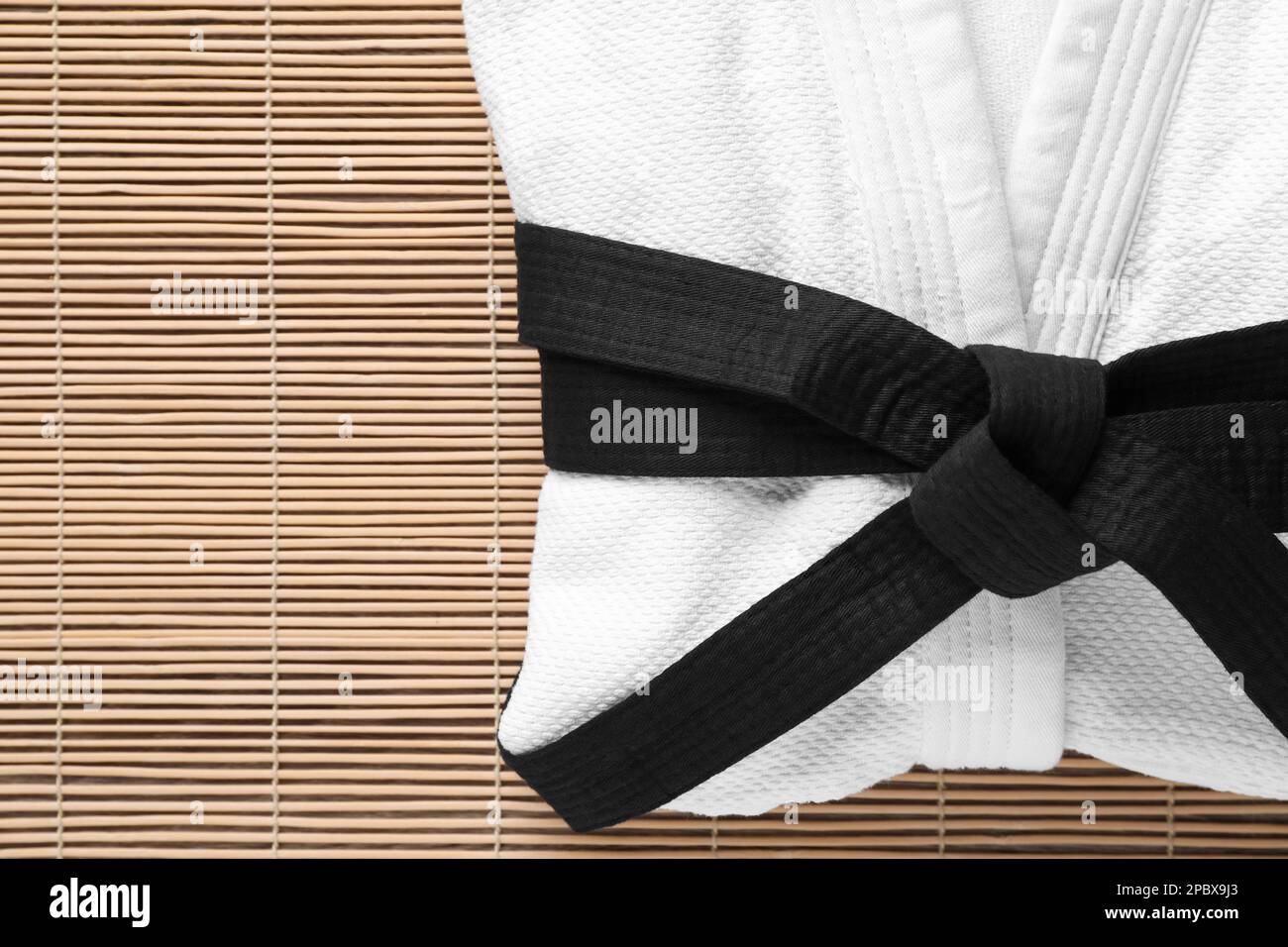 Martial arts uniform with black belt on bamboo mat, top view. Space for ...