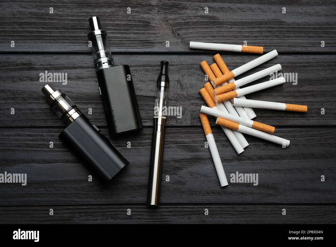 Cigarettes and different vaping devices on black wooden background ...