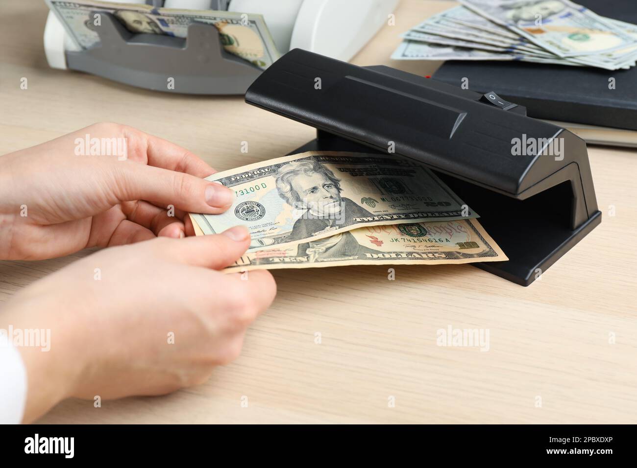 Woman checking dollar banknotes with currency detector at wooden table ...