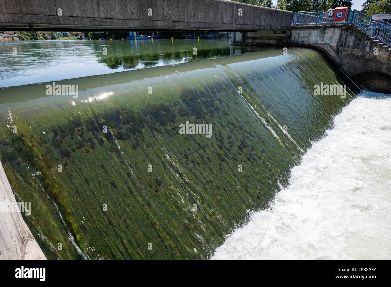 Shallow river water flowing down a cement dam in Europe. Day time, foaming water, no people ...