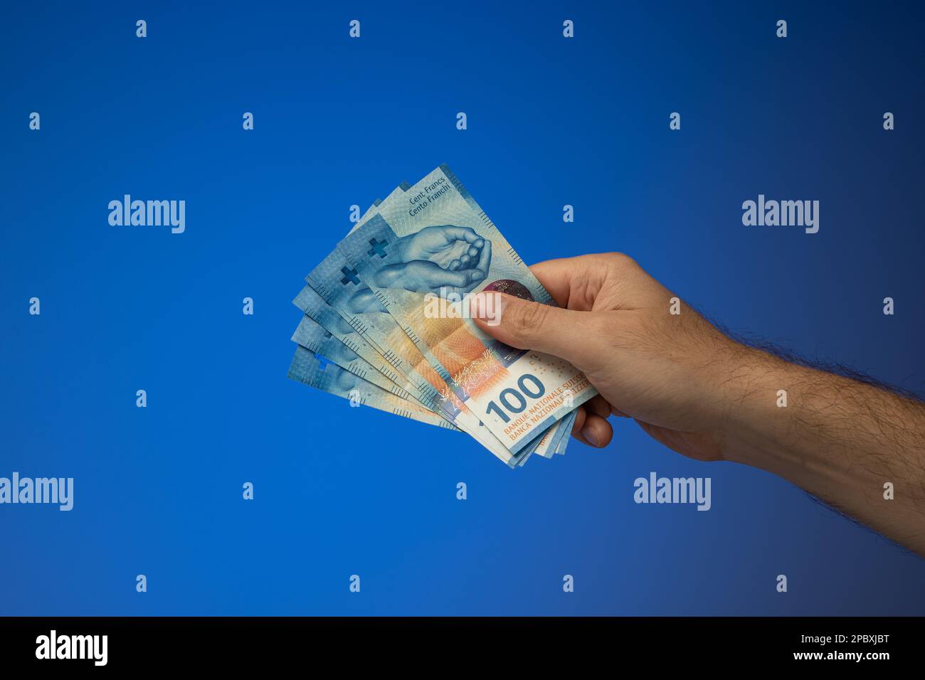 A spread of 100 Swiss Francs banknotes, held in hand by a Caucasian ...
