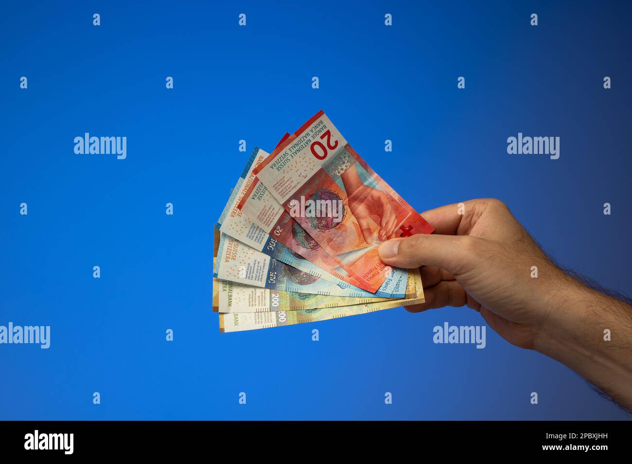 A spread of 20, 100 and 200 Swiss Francs banknotes, held in hand by a ...