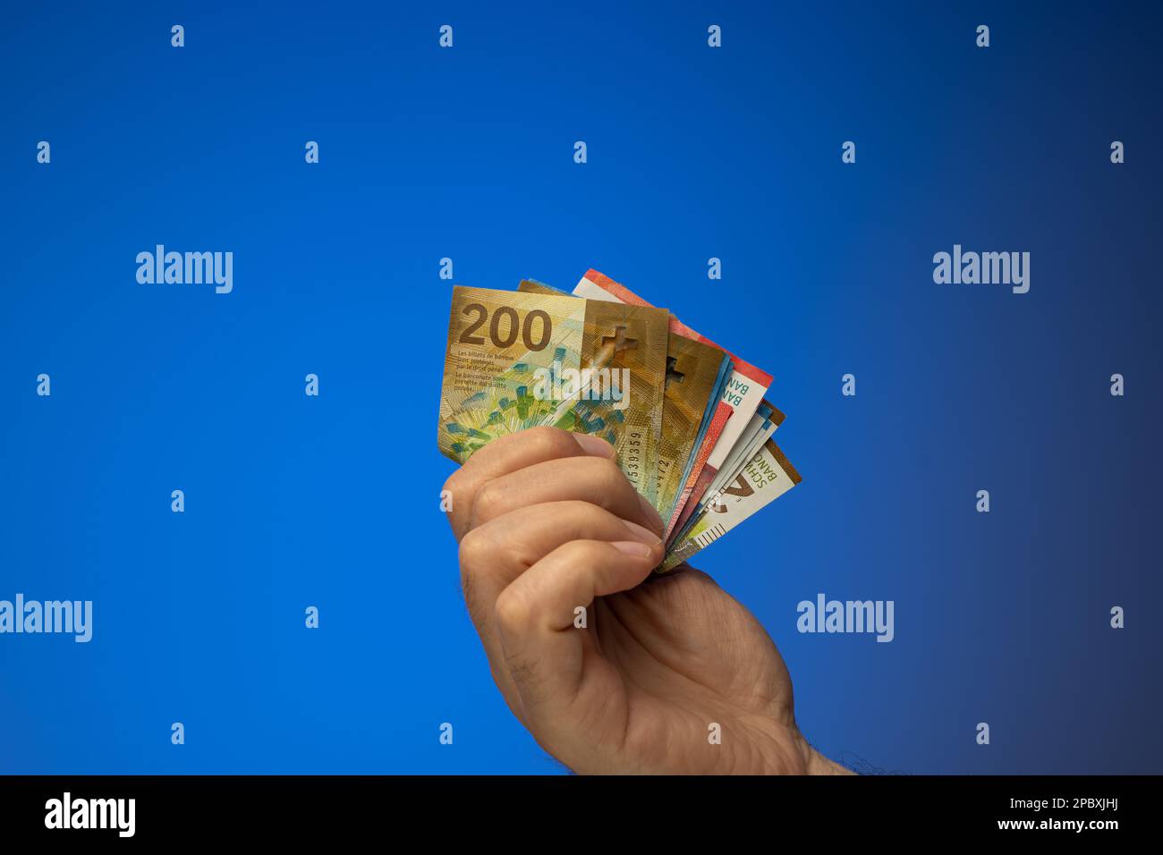 A spread of 20, 100 and 200 Swiss Francs banknotes, held in hand by a ...