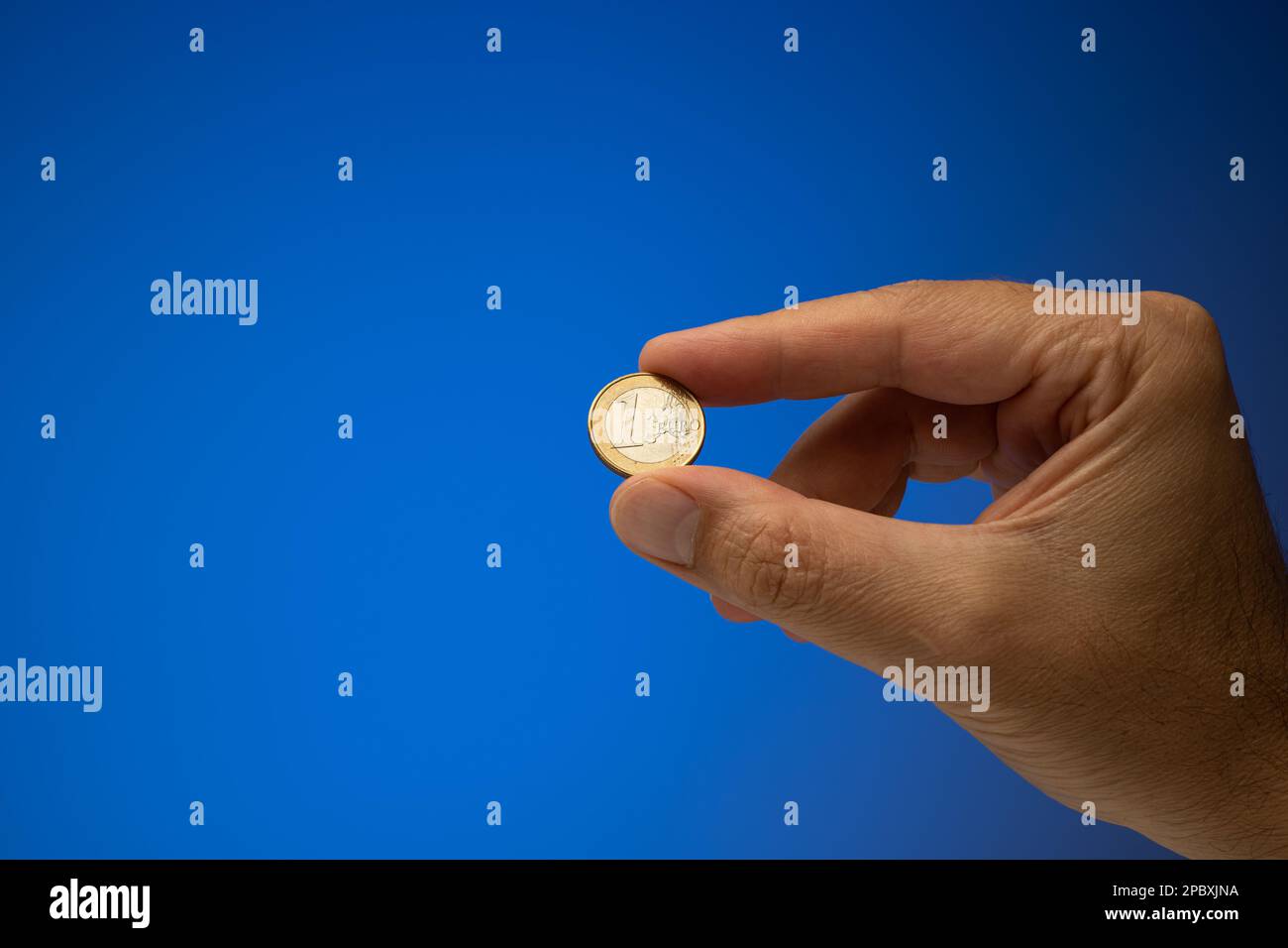 1 Euro metal coin, held in hand by a Caucasian male. Close up studio ...