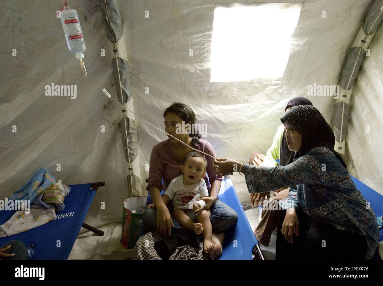 An Indonesian family tends to a sick baby in a tent set up outside an ...