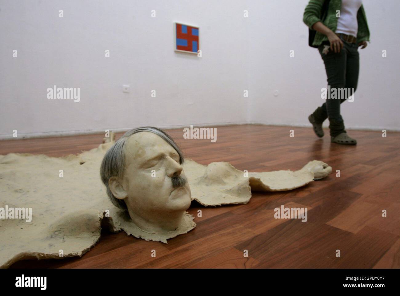 A visitor walks away from a framed paintings of swastika and a rug made ...